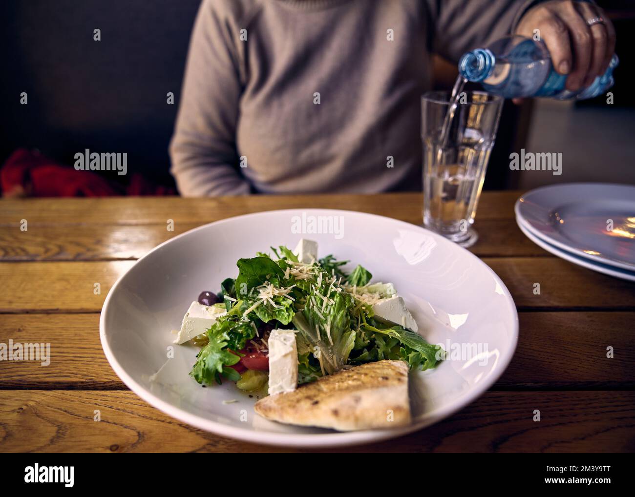 Green salad with feta cheese in a white ceramic plate and a woman pours ...