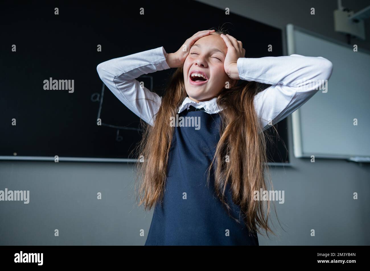 Caucasian girl stands at the blackboard holding her head with her hands ...