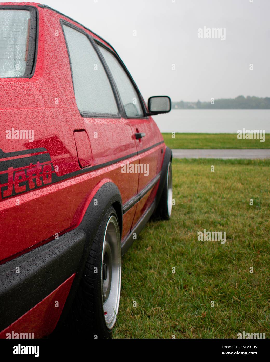 A wet red Volkswagen Golf Mk2 car at a car meet outdoors on green grass ...
