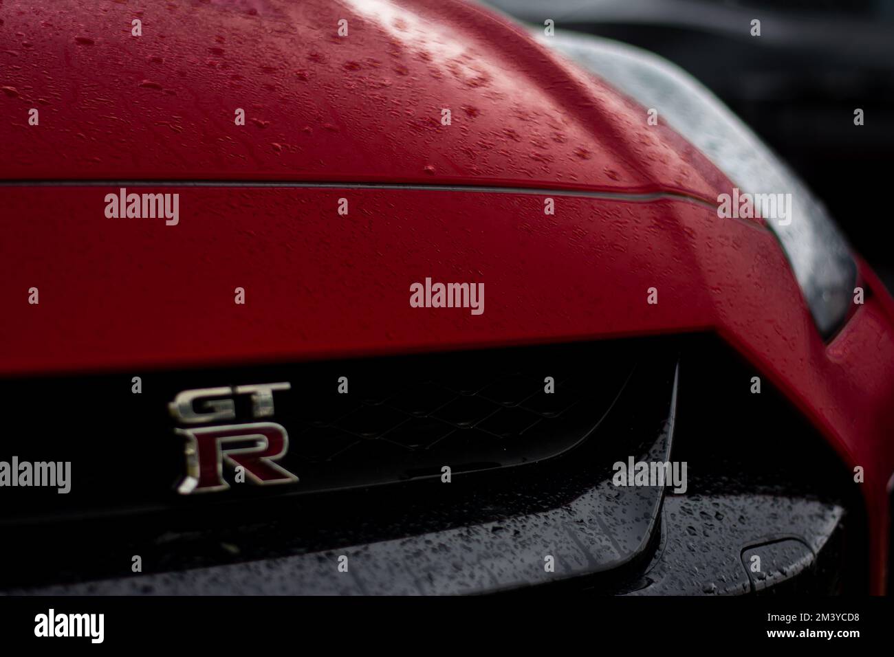 A closeup of the front and logo of wet red Nissan GT-R sports car at a ...