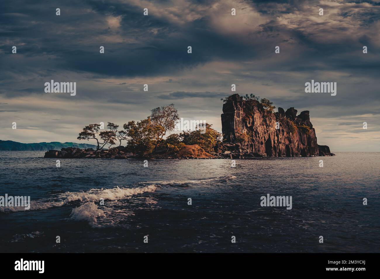 A small island seen from the shore with rock formation and few trees ...