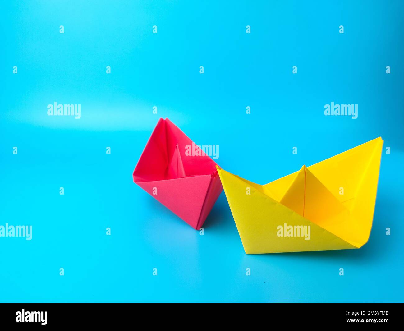 A big red paper ship and smaller yellow one on turquoise background ...