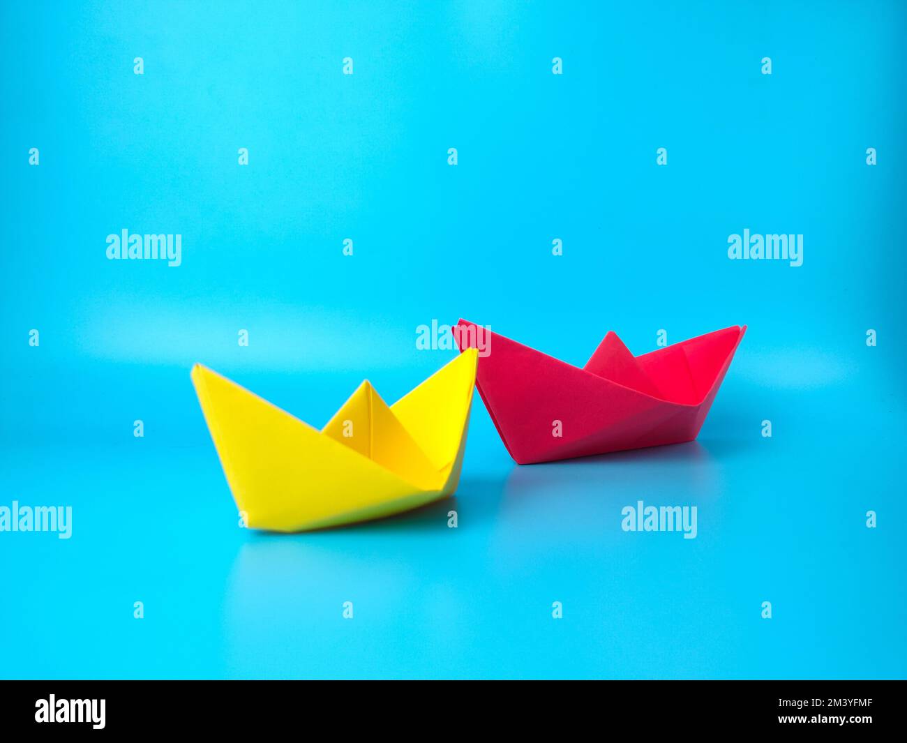 A big red paper ship and smaller yellow one on turquoise background ...