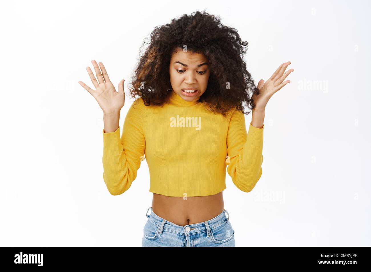 Portrait of shocked young woman, drop something down, raising hands up ...