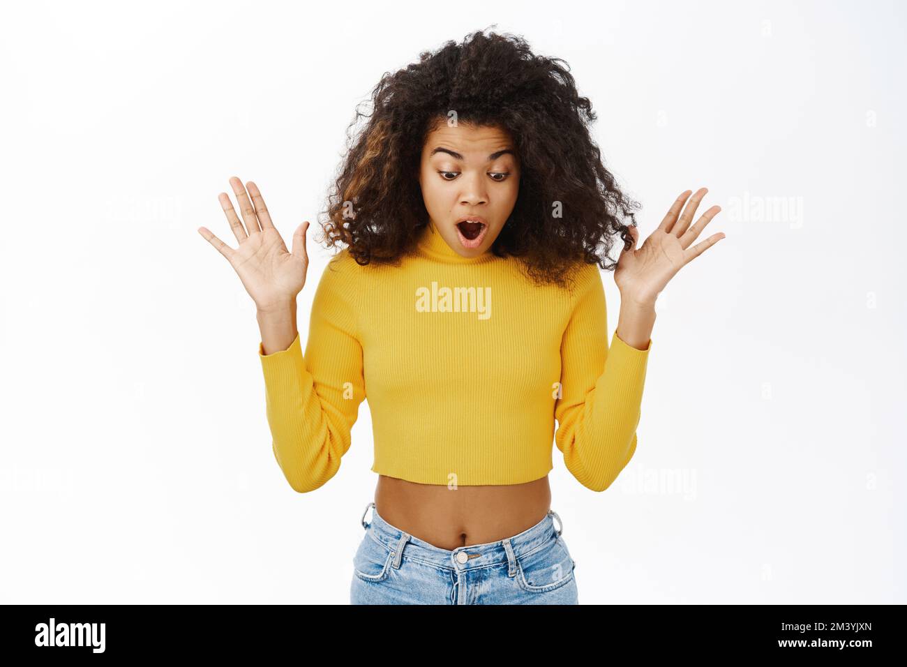 Portrait of shocked young woman, drop something down, raising hands up ...
