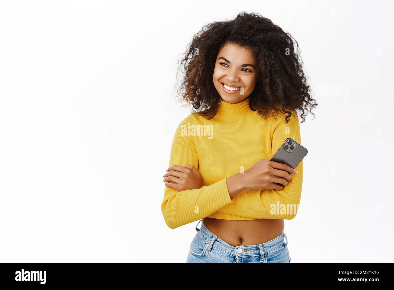 Confident smiling Black girl, holding mobile phone, standing with ...