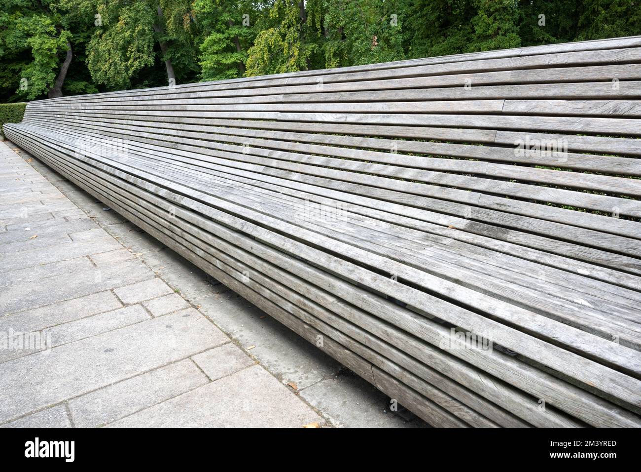 An unusually long park bench made of very long wooden decks with leafy ...