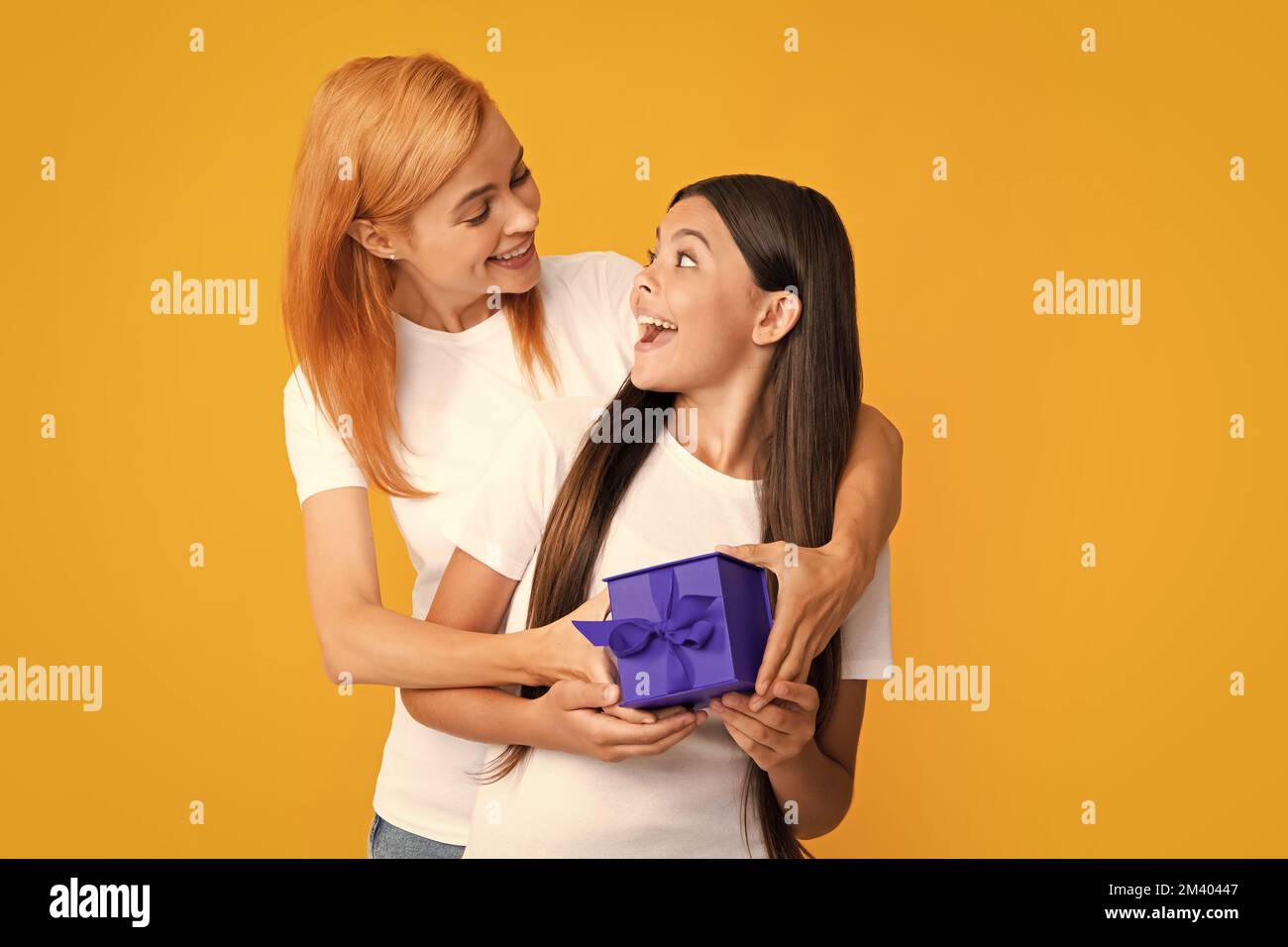 Mother and daughter with present gift. Teenager girl giving gift box to her mother on yellow ...