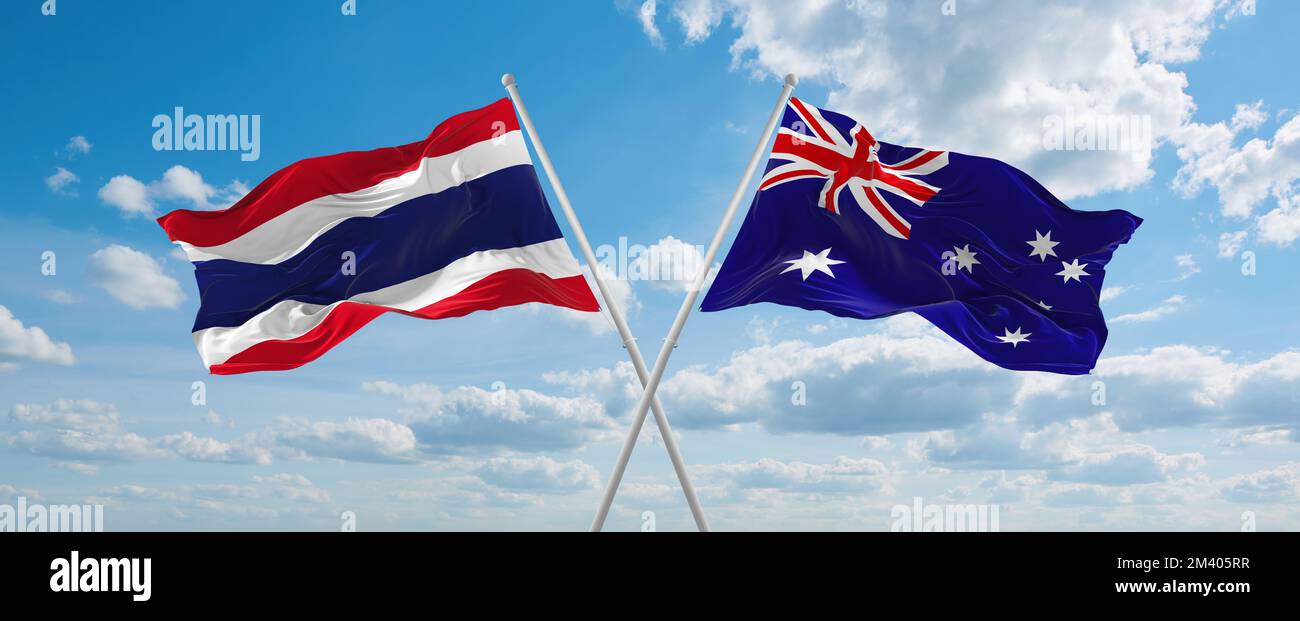 two crossed flags Australia and Thailand waving in wind at cloudy sky ...