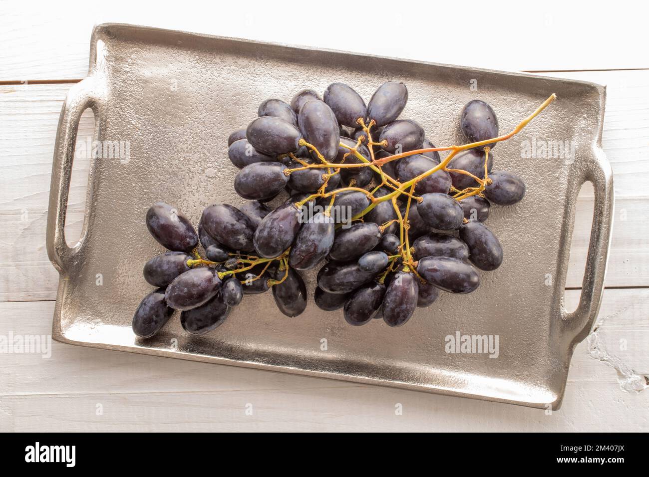 One bunch of juicy organic black grapes on a metal tray on a wooden ...