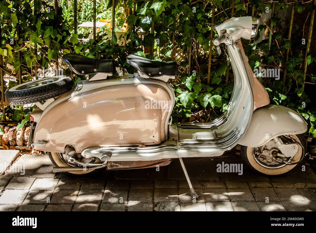 A closeup shot of a beige vintage scooter, in a shadow on a sunny day ...