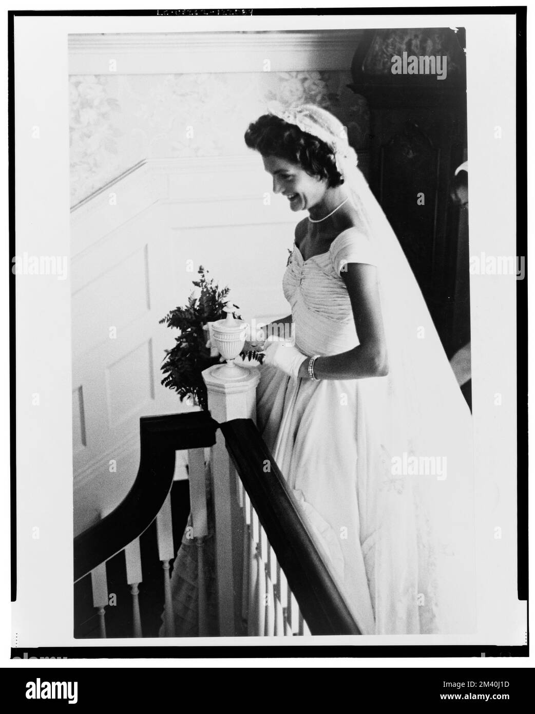 Jacqueline Bouvier, in wedding attire, gazing down from stair landing ...