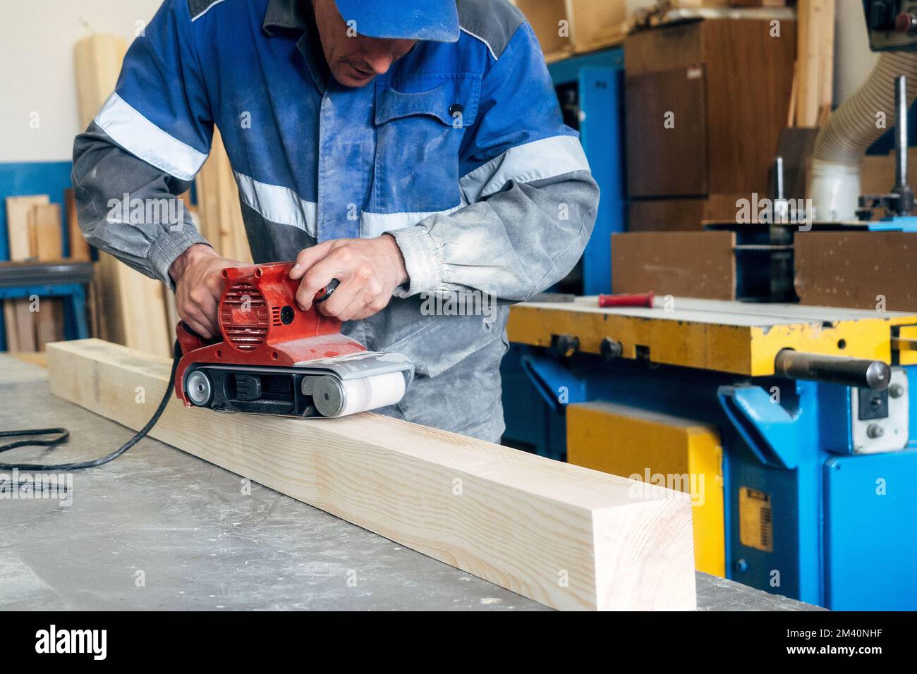 Carpenter in work clothes processes wood with grinder. Polishing of ...