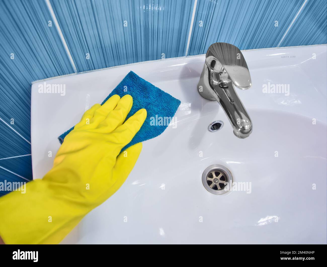 Hand in yellow rubber glove with rag wipes white sink. Cleaning and ...