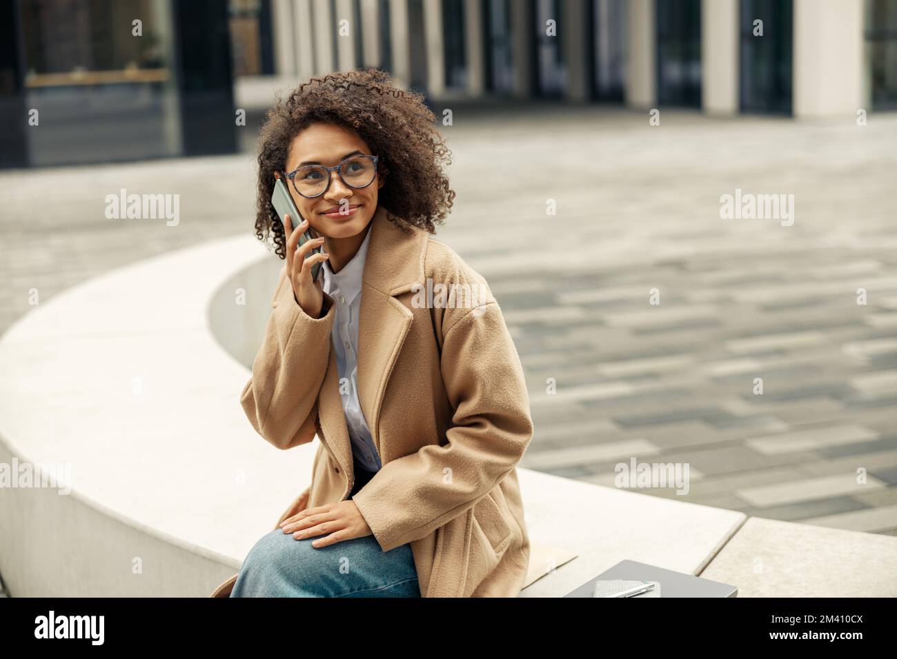 Smiling afro american businesswoman talking phone while sitting on ...