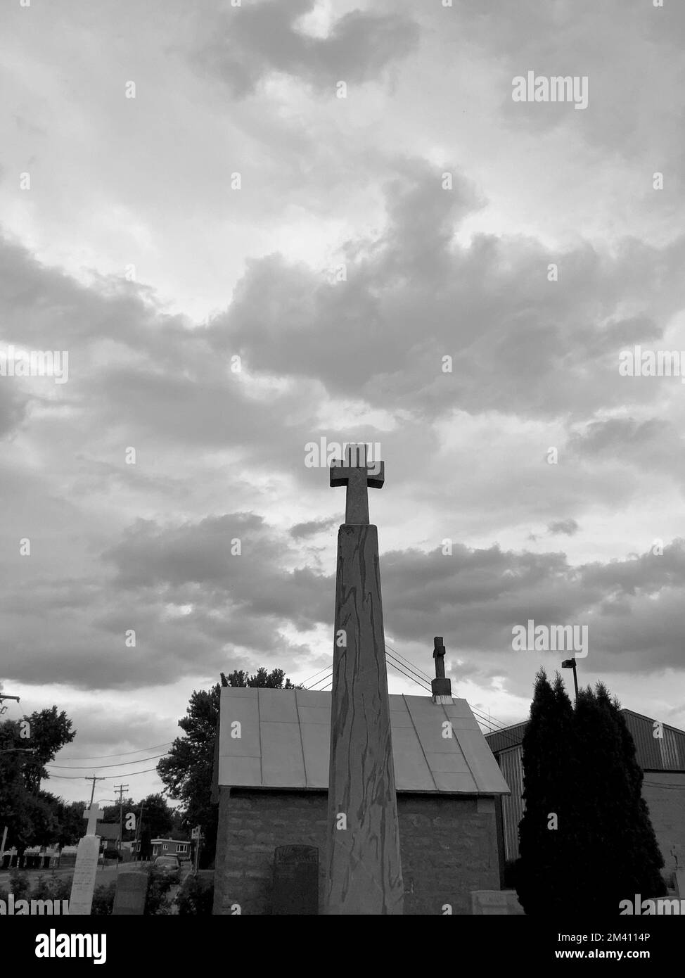 A grayscale vertical shot of a cross tombstone under cloudy sky in a ...