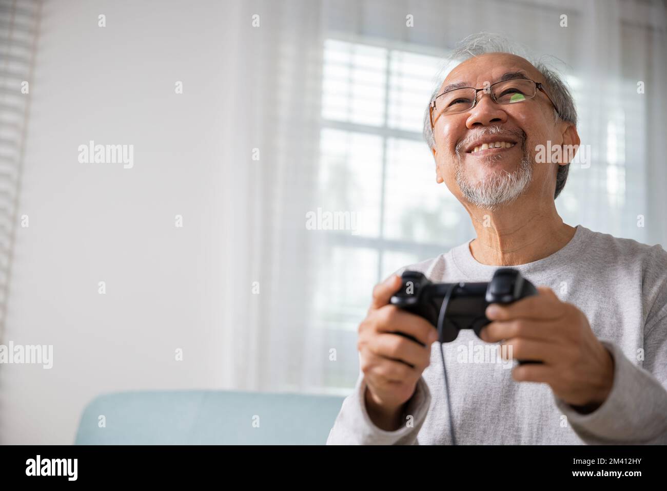 Asian senior old man enjoying holding joystick playing video game at ...