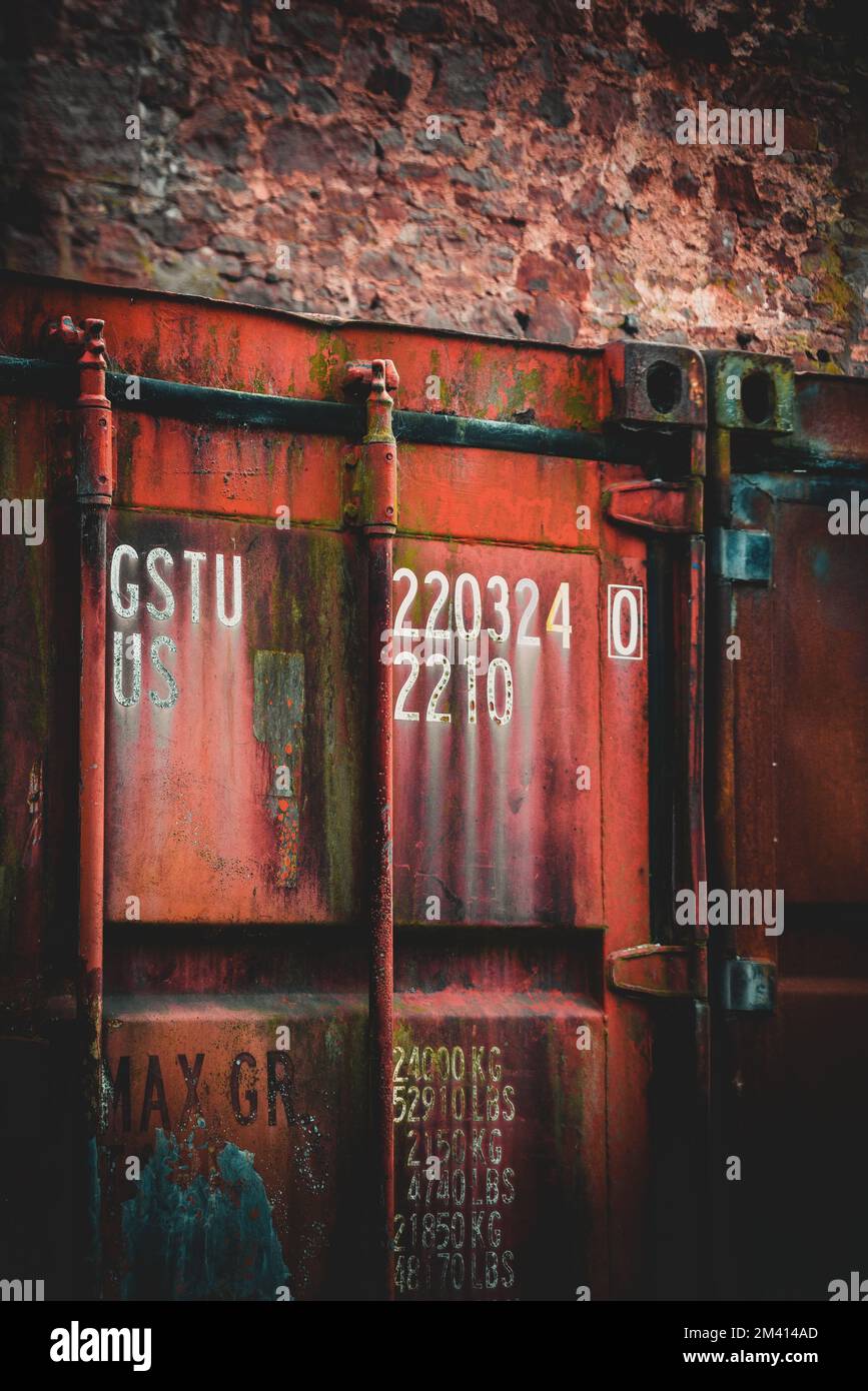 A vertical shot of old red rusty shipping container door with technical ...