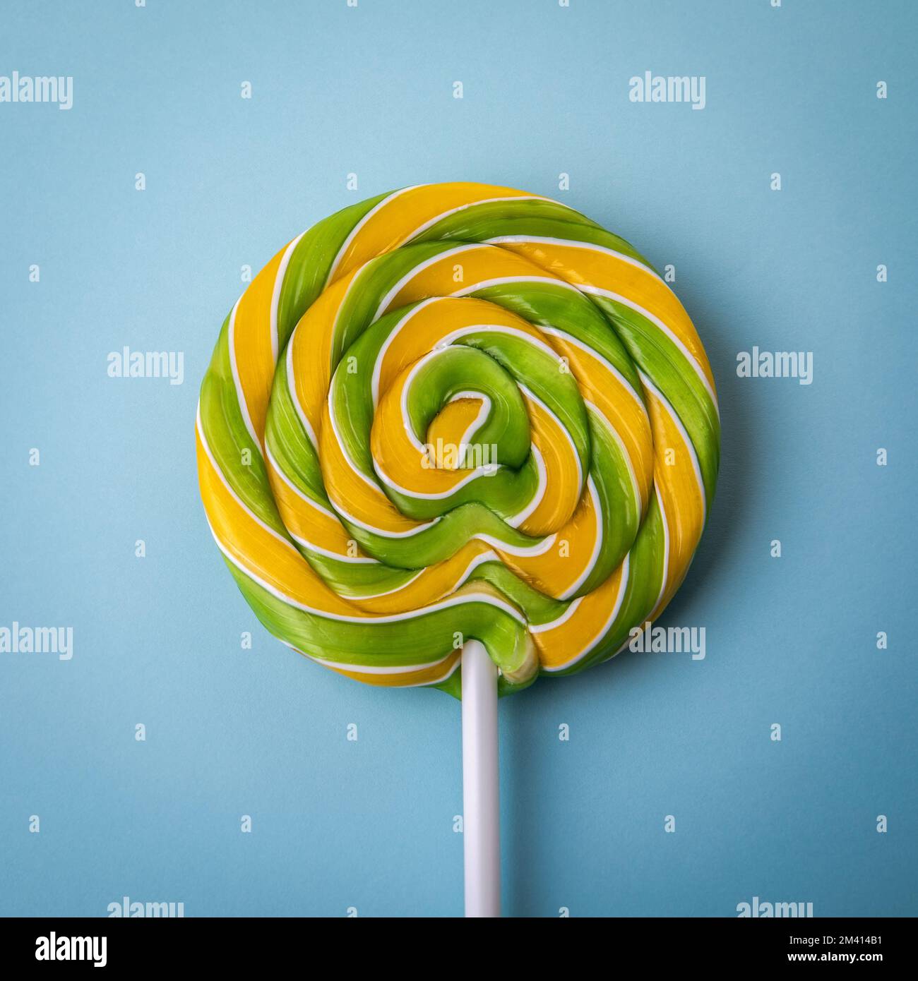 Colorful green-yellow candy, lollipop on a stick on a blue background ...
