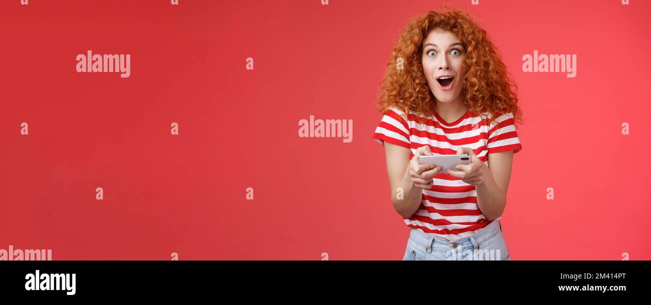 Impressed excited good-looking redhead curly woman hold smartphone ...