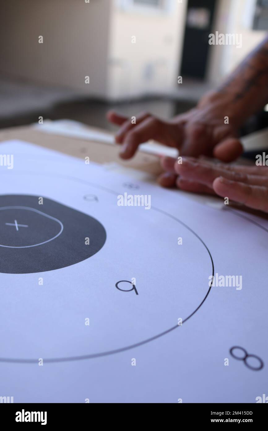 A person pointing at pilot holes of shooting target paper on table with ...