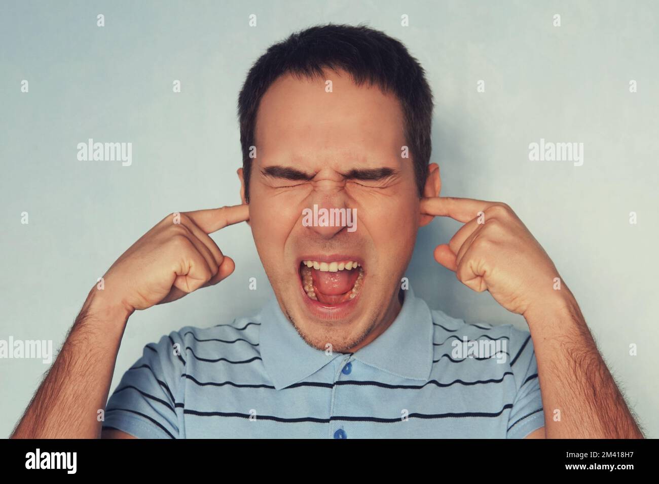 Stressed frustrated young man plugging his ears with fingers and ...