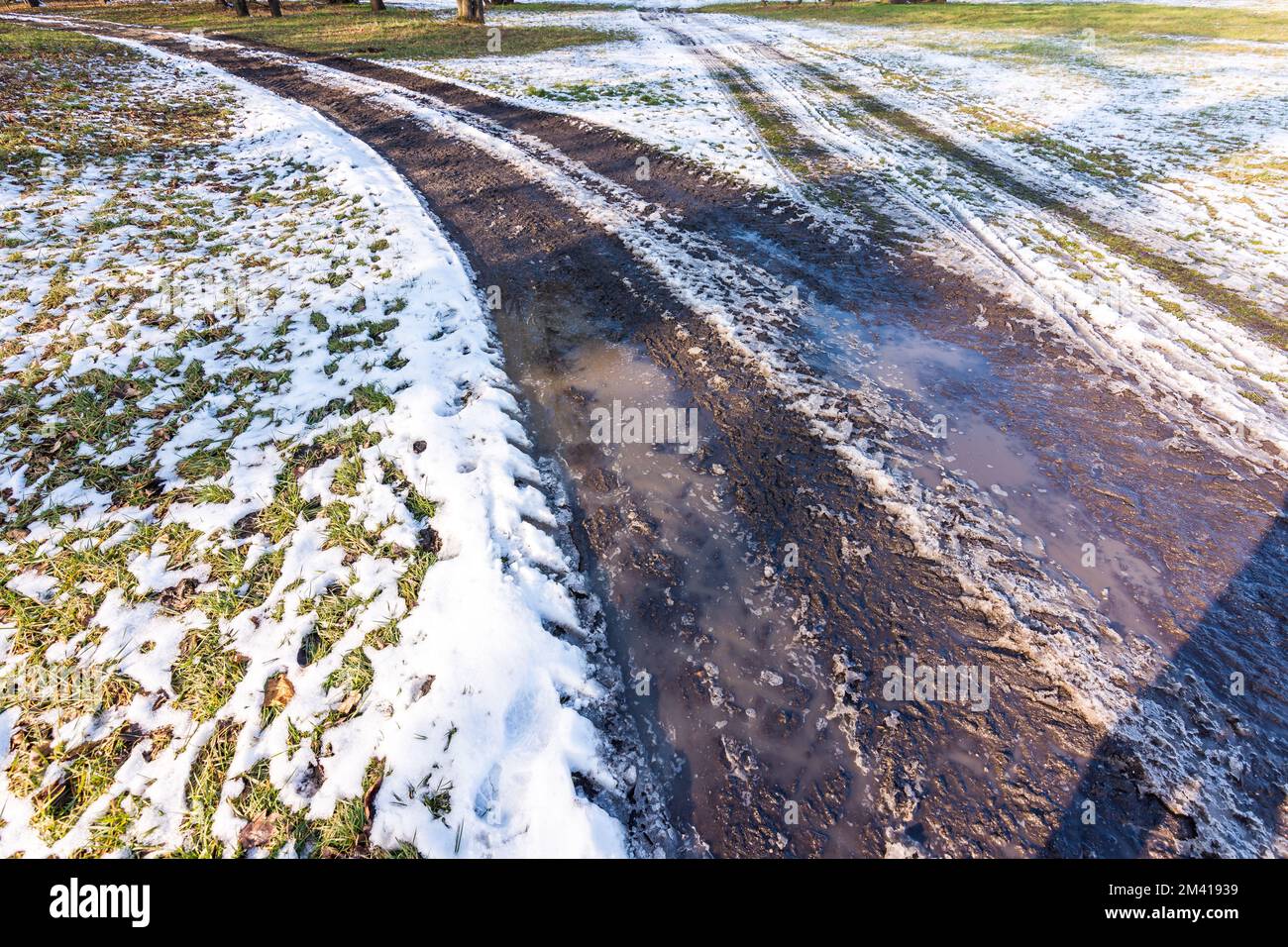Small puddle on the road, reflection in water near the meadow. Snow and ...