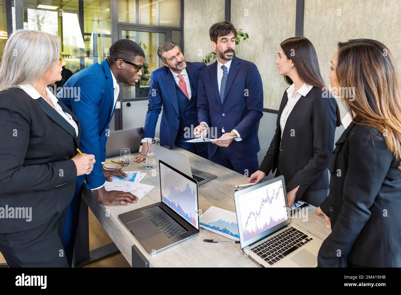 Group of multiracial colleagues in formal wear discussing graphs and planning work while ...