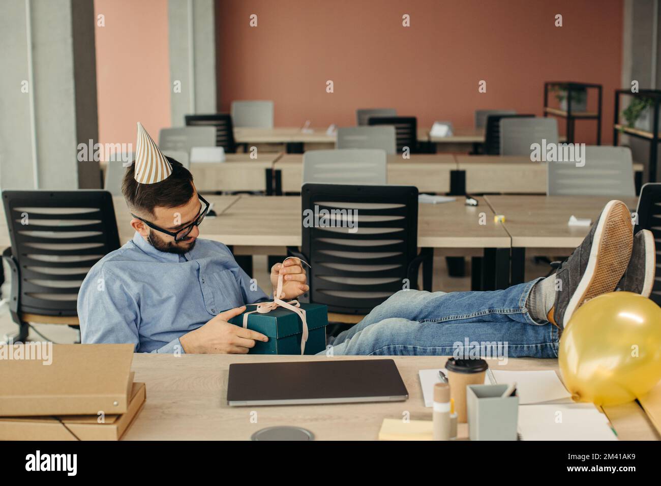 Happy positive male office worker with beard in cone hat holding gift ...