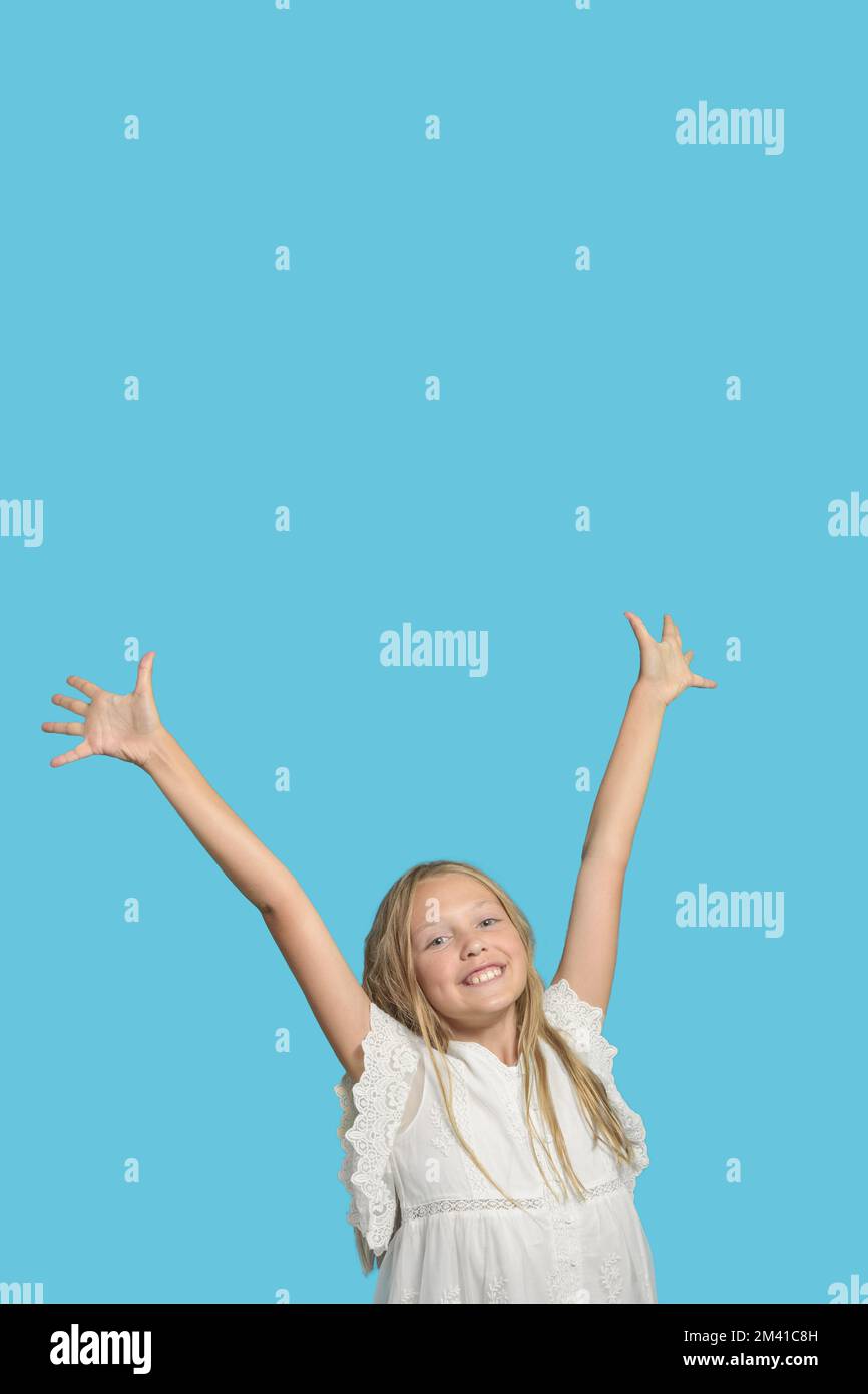 Childhood happiness. Smiling young girl rise her hands up to the sky ...