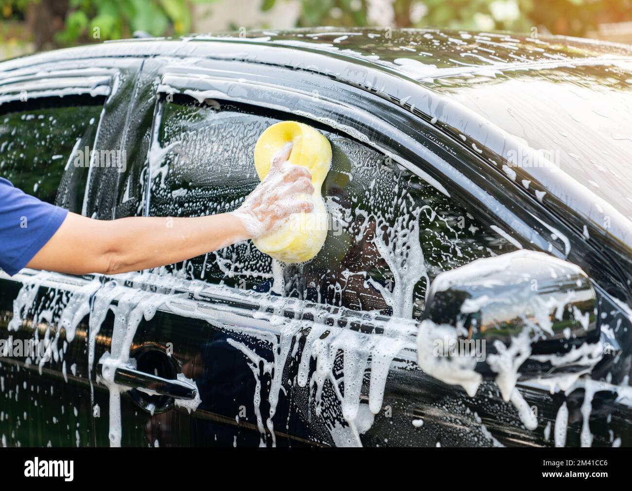 Hand of yellow sponge washing car window at her home. Car detailing ...