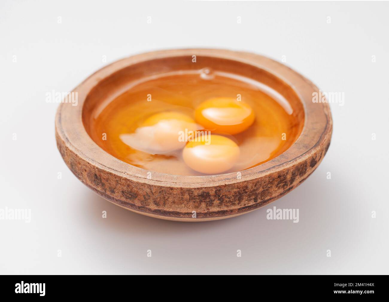 Three egg yolks in wooden plate on white background Stock Photo - Alamy
