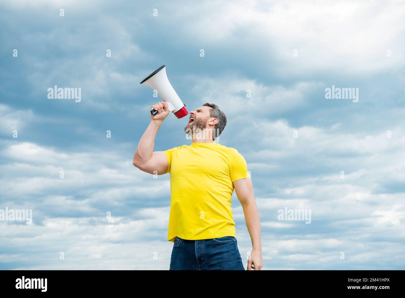 man in yellow shirt shout in megaphone on sky background. communication ...
