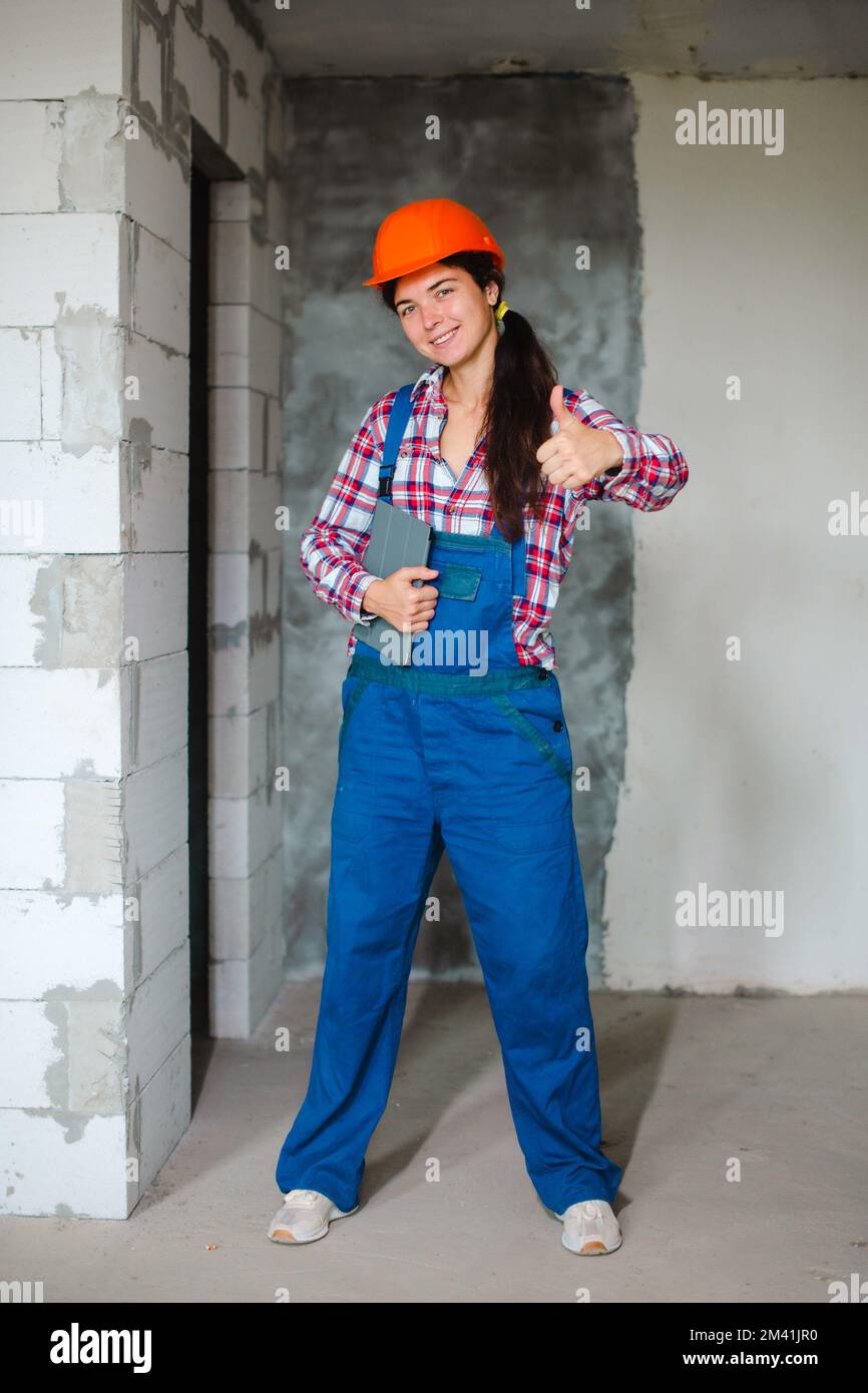 woman builder in blue overalls thumbs up gesture and check project in ...