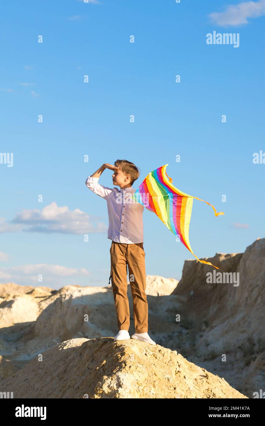 A 9-year old boy with bright colorful kite stands high on a mountain ...