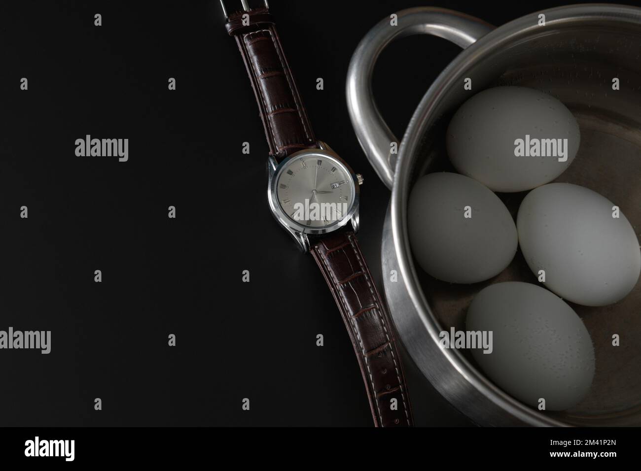 Wrist watch and cooking boiled eggs in a saucepan. On a black ...
