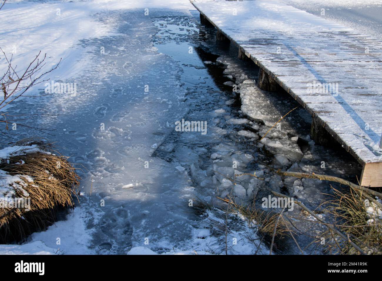 Broken thin ice on a lake beside a pier covered with snow Stock Photo ...