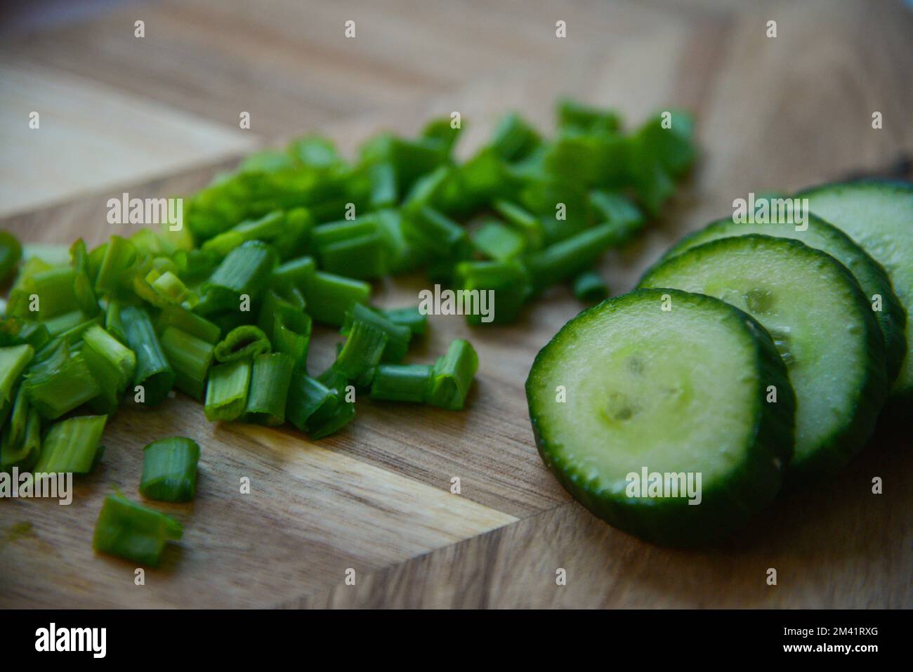 green fresh sliced onions with green sliced cucumber on a wooden board ...