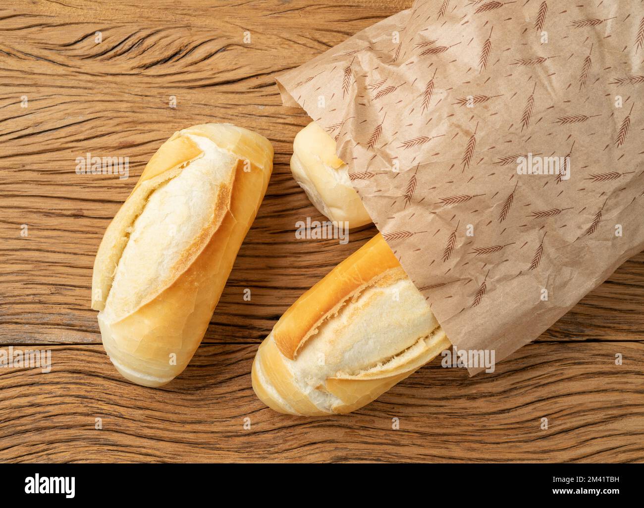French bread, salt bread or pistolet on a paper bag over wooden table ...