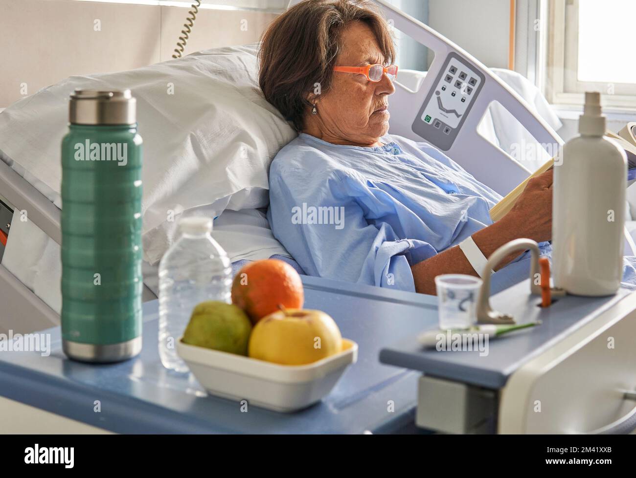 senior lady in the hospital room sitting on the stretcher reading a ...