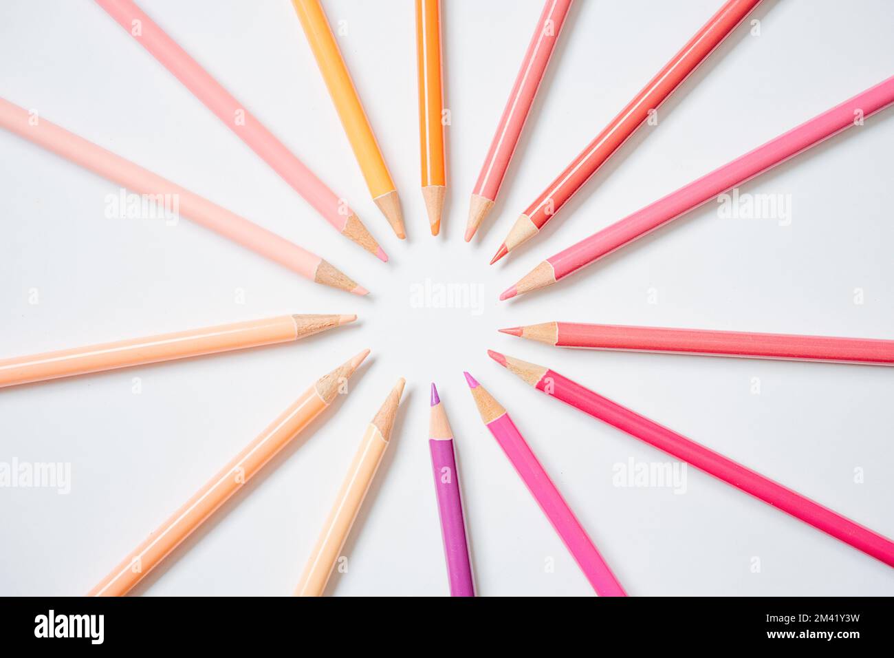 Composition of warm colored pencils paced in solar pattern over white ...