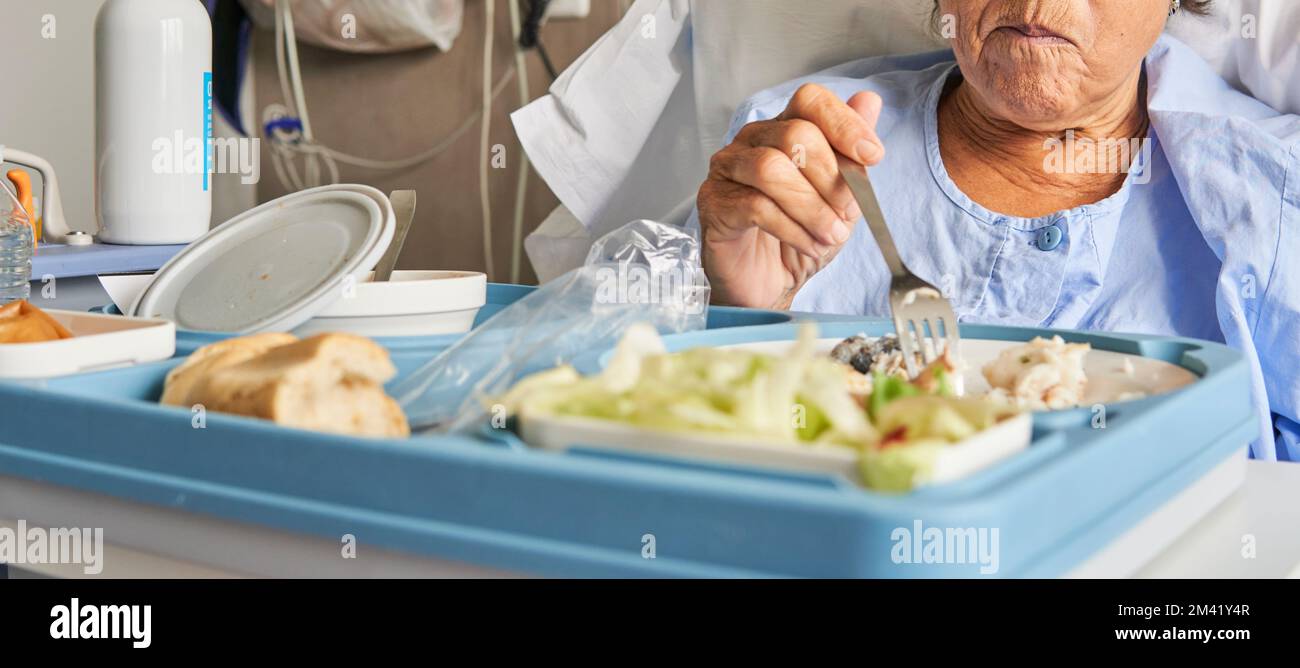 senior lady in the hospital room sitting on the stretcher having lunch ...