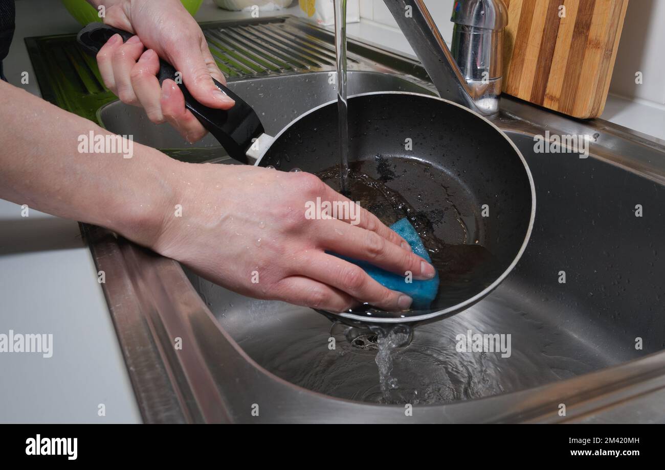 woman washes a frying pan in the kitchen under running water Stock ...