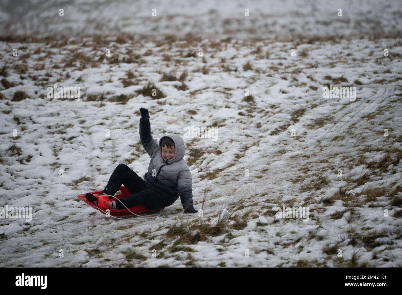 A sledger makes the most of the snow on an icy and snowy hill as rain ...