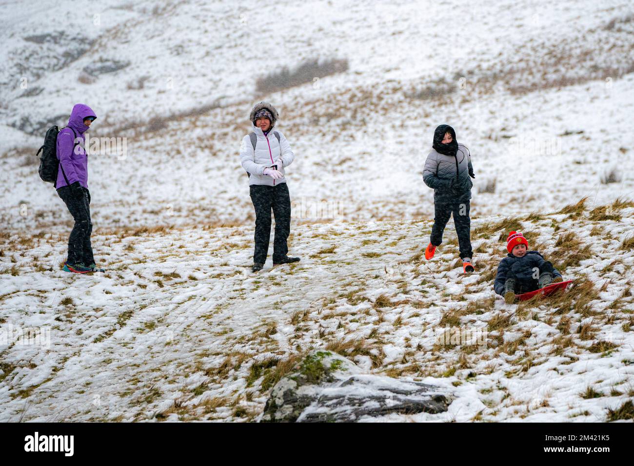 People make the most of the snow on an icy and snowy hill as rain falls ...