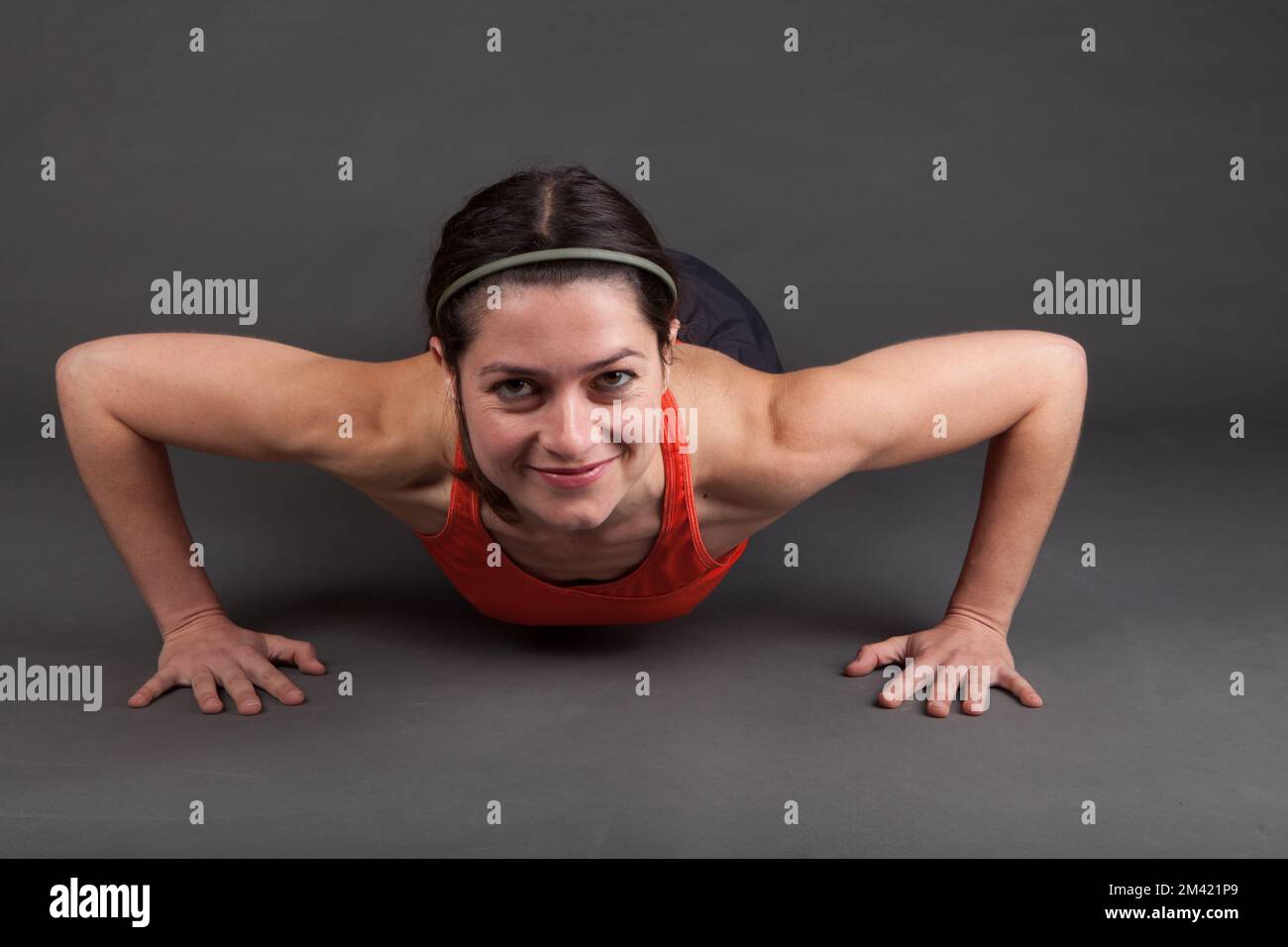 shot of a fit muscular woman doing a pushup on grey with room for copy ...