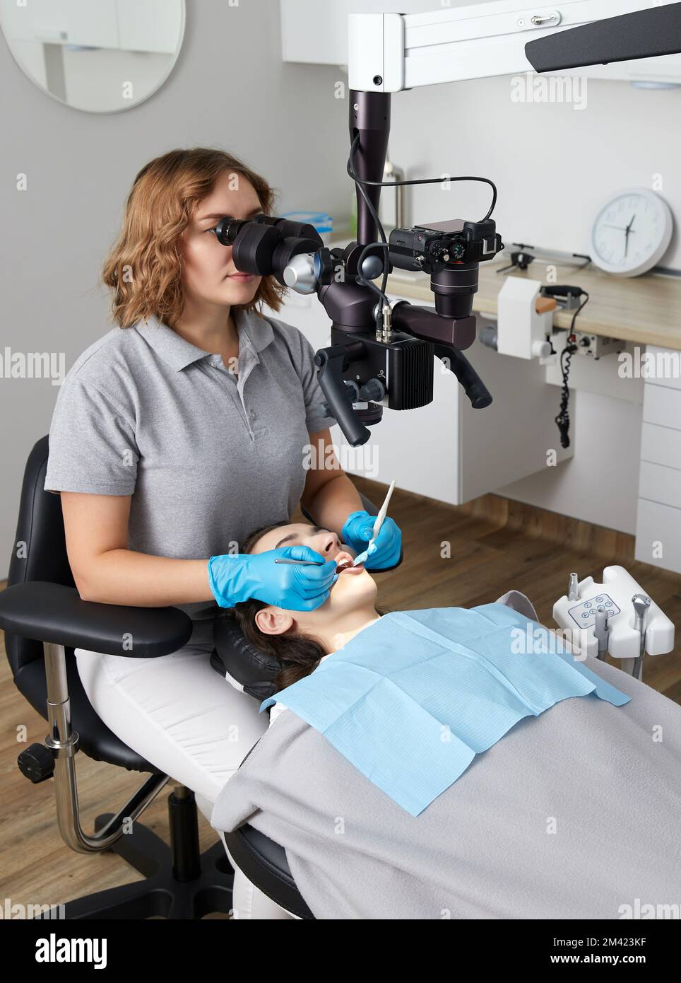 Female dentist with microscope treating patient teeth at dental clinic ...