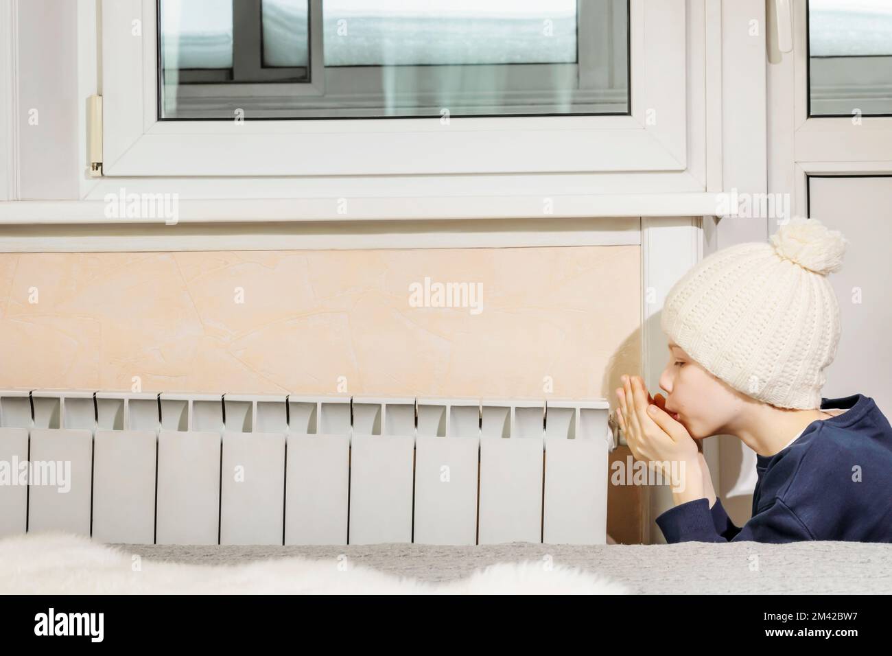 Winter, heating season. Teenage boy in warm clothes and hat, warming ...