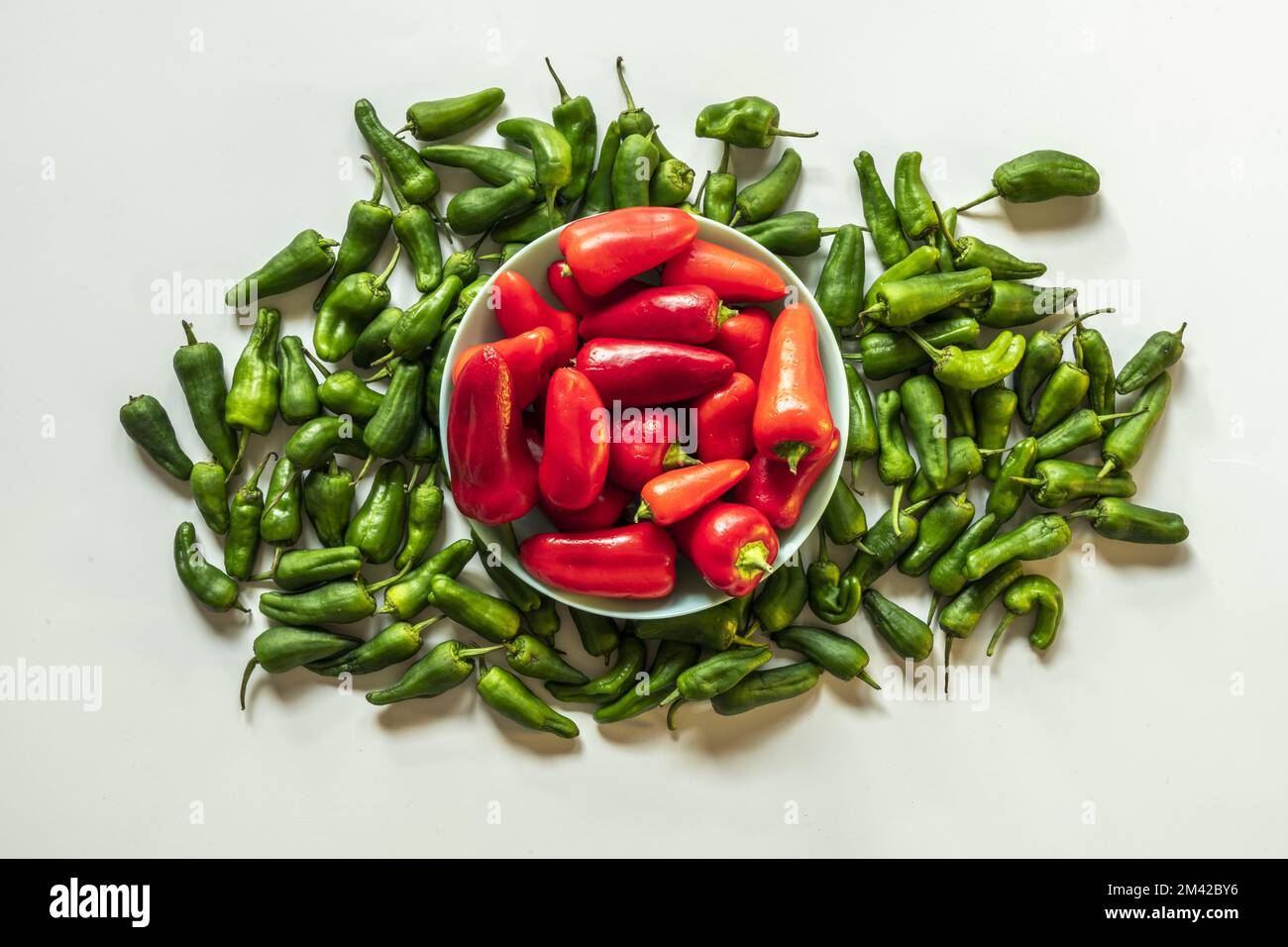 A beautiful still life with a white surface with lots of green peppers ...