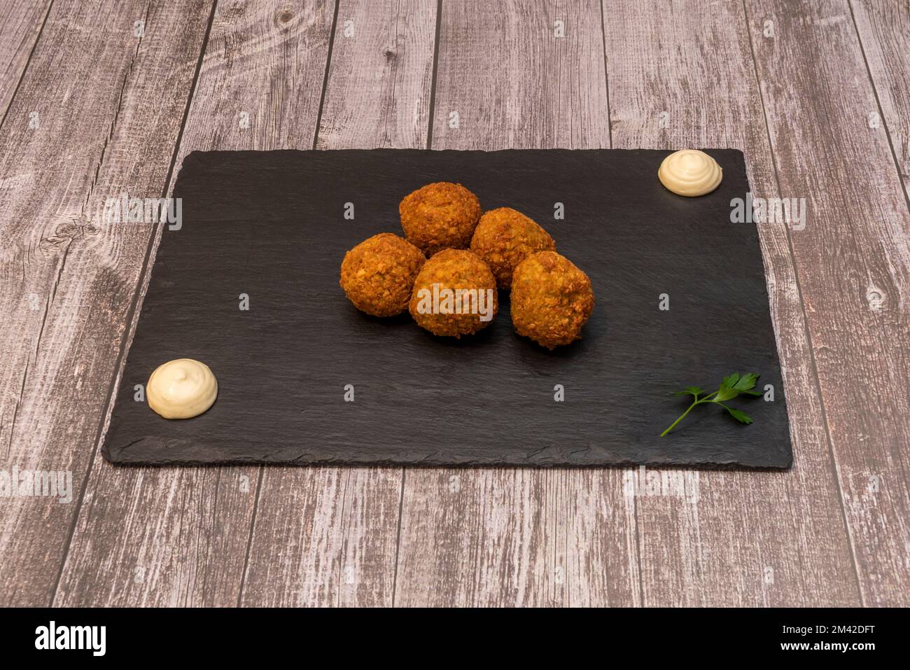 Plate of falafel in fried balls on black slate plate with sauces and ...
